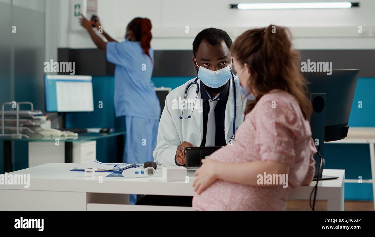 General practitioner using digital tablet at appointment with pregnant ...