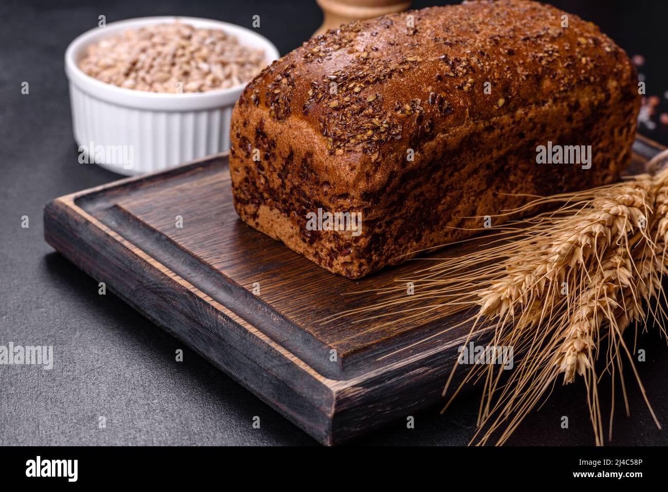 Fresh baked brown bread with ears and grains of wheat on a dark ...