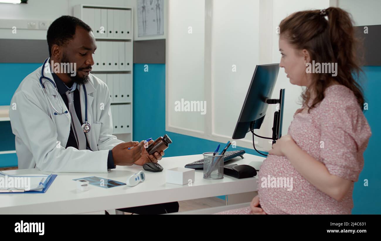 Male obstetrician giving bottle of pills to woman with baby bump ...