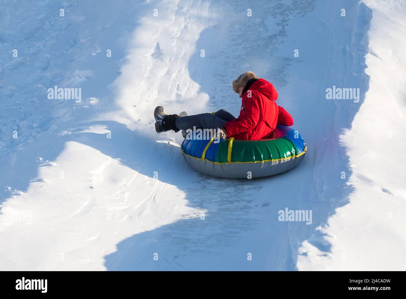 A girl rides a tube from a slide in winter in a snowfall. Tubing ...