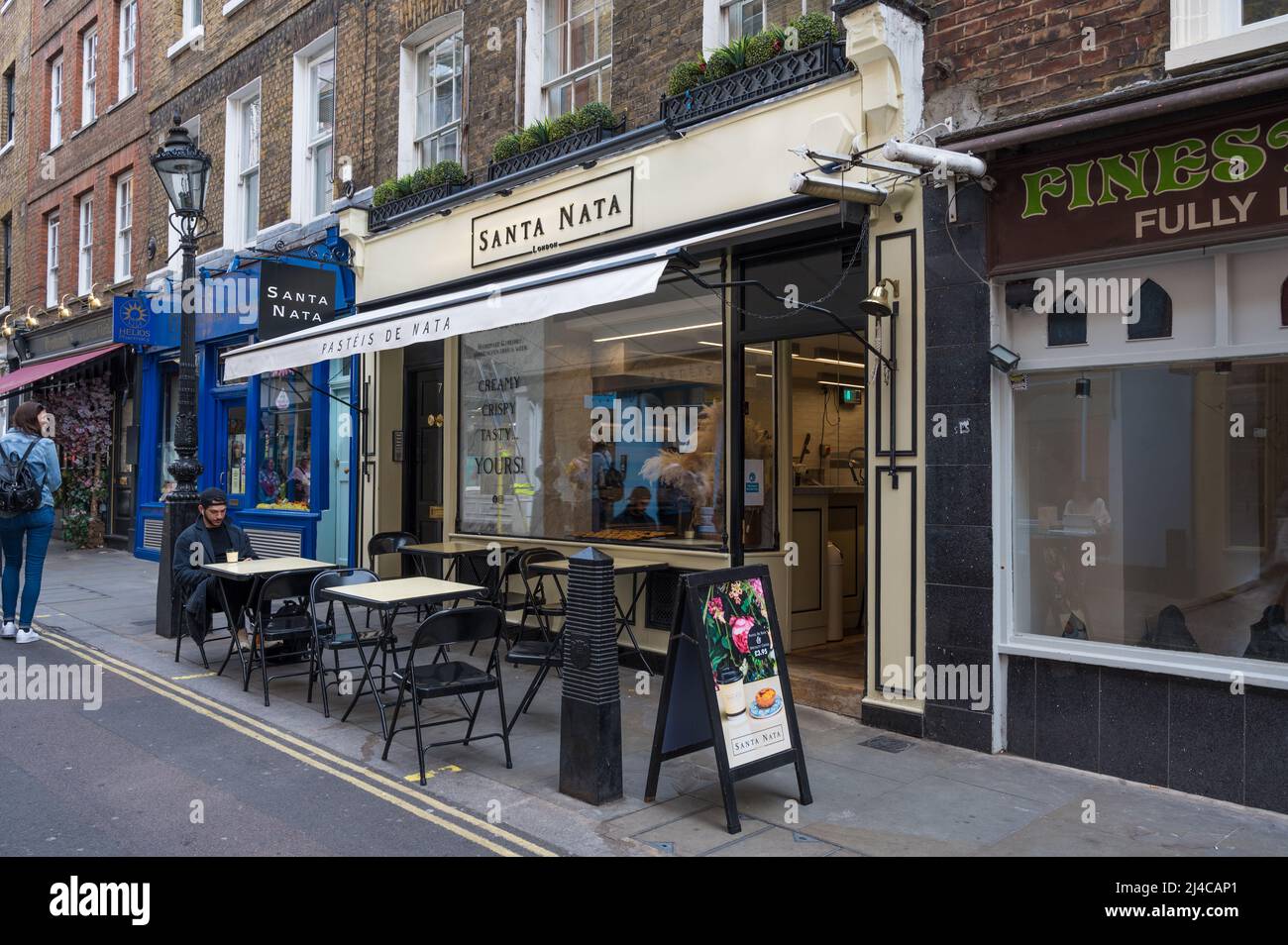 A lone young man seated at pavement table outside Santa Nata, a shop ...
