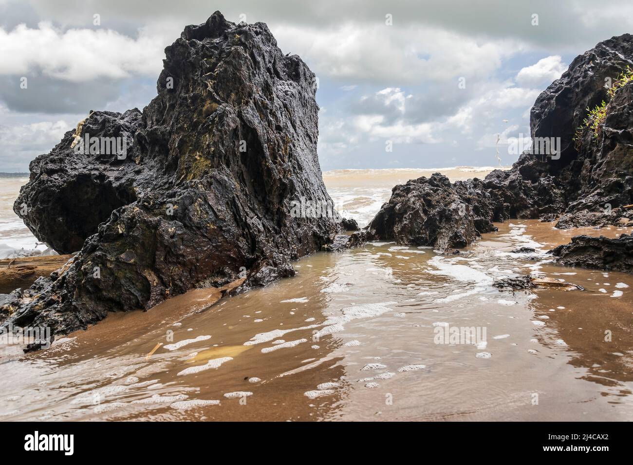 Black dark boulders lying on a beach after the coast in Axim Ghana West ...