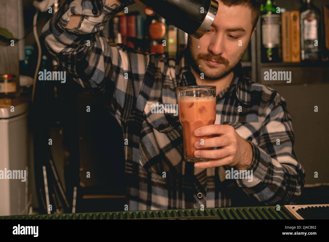 Bearded bartender pouring cocktail from shaker into highball glass ...