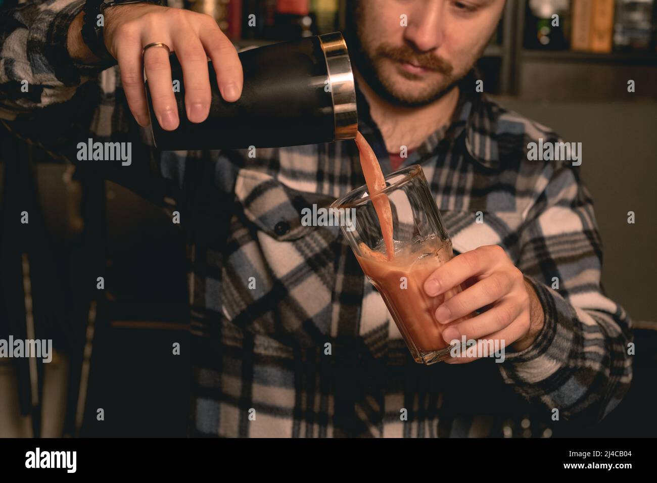 Bartender pouring cocktail from shaker into tall glass with ice Stock ...