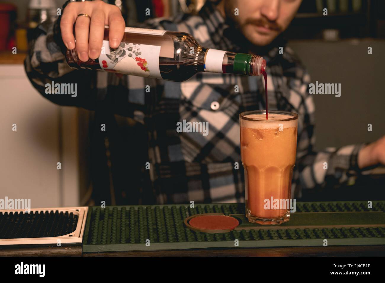 Bartender preparing Tequila Sunrise cocktail, adding pomegranate syrup ...