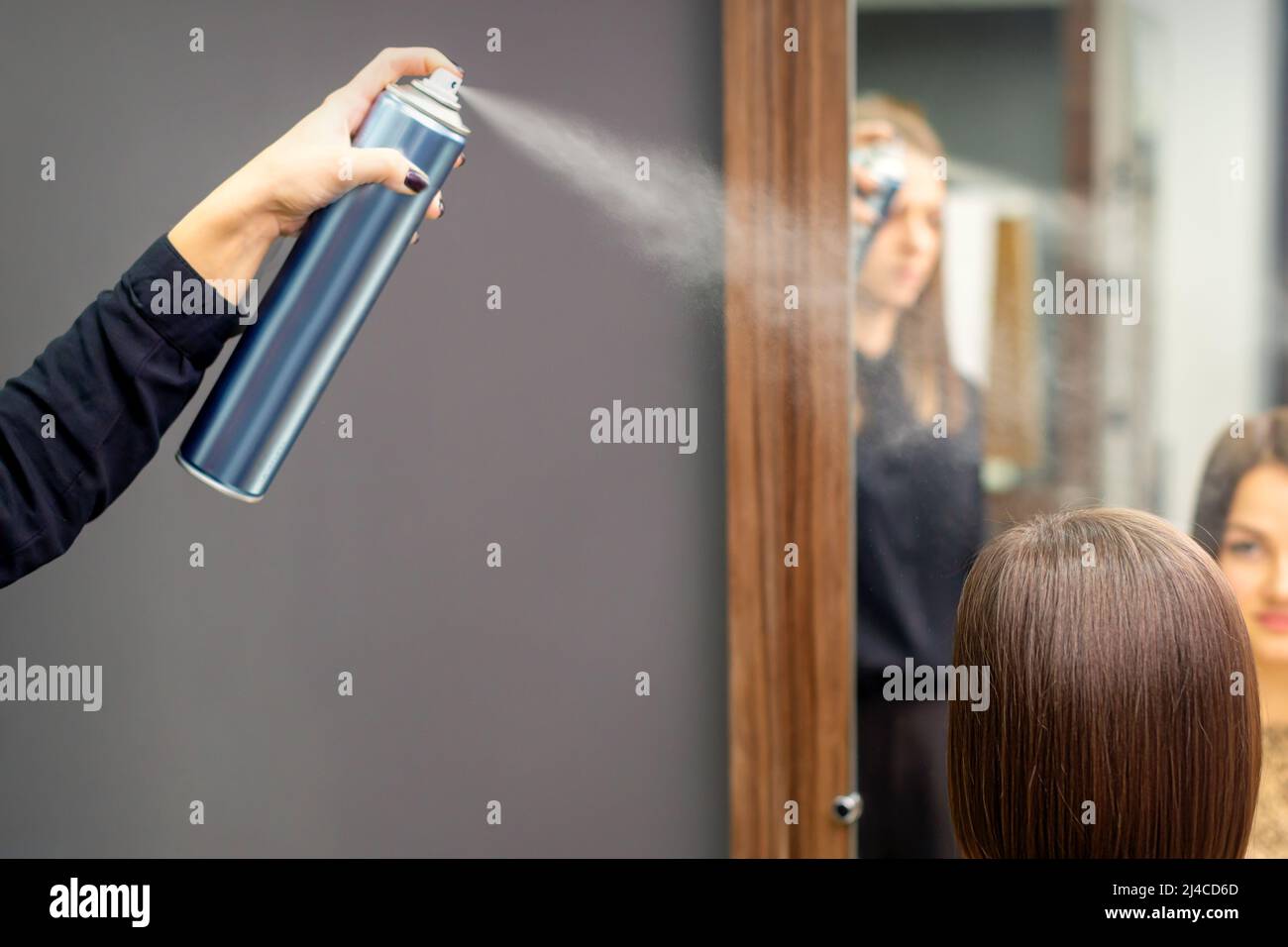 A hairdresser is using hair spray to fix the short hairstyle of the ...
