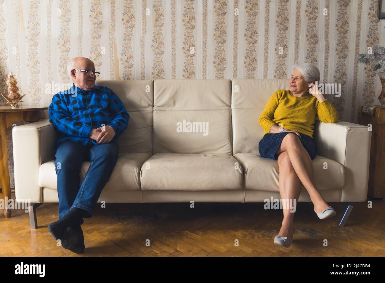 Elderly Upset Married Couple Sitting Apart On Leather Sofa In Their Old