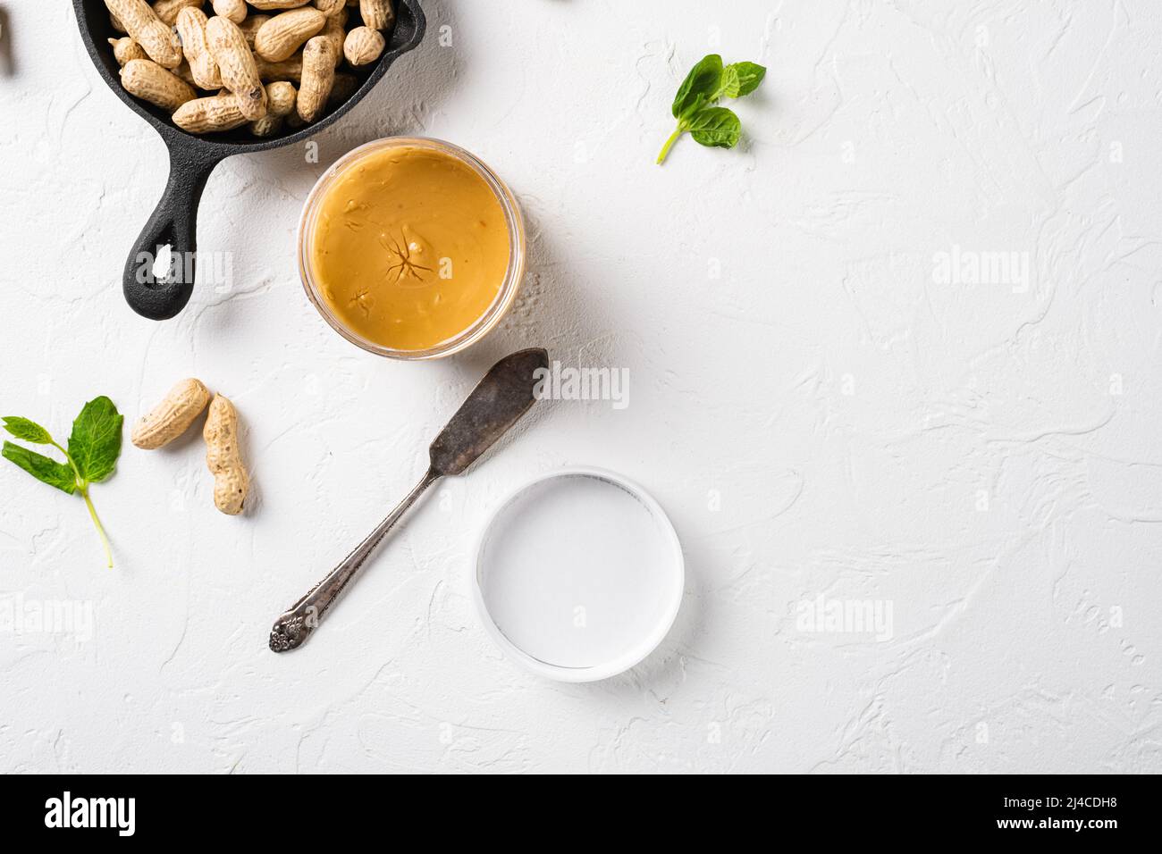 Peanut paste in an open jar and peanuts set, on white stone table ...
