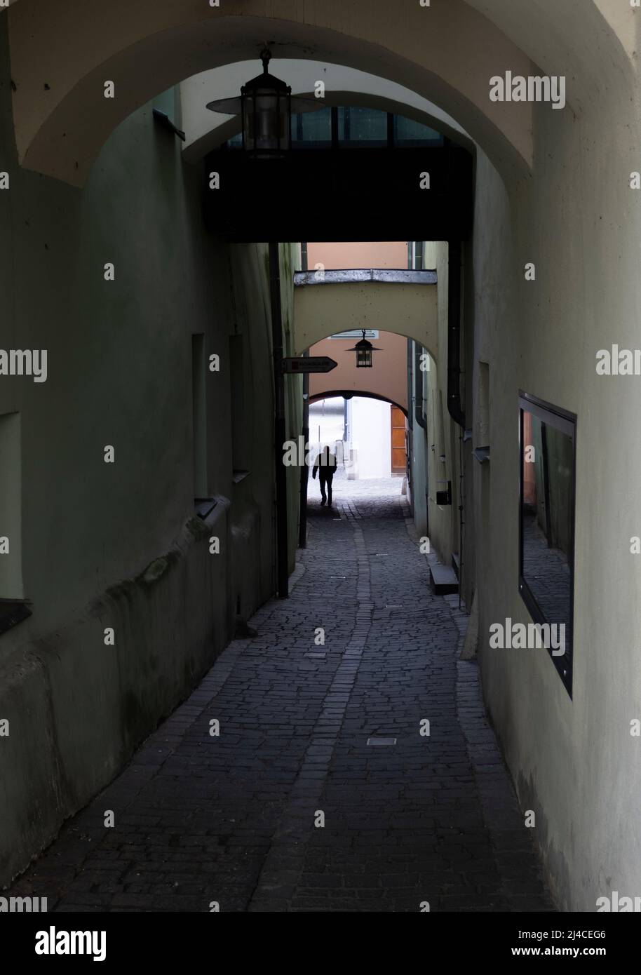 Silhouette of a man walking between houses along a narrow cobbled ...