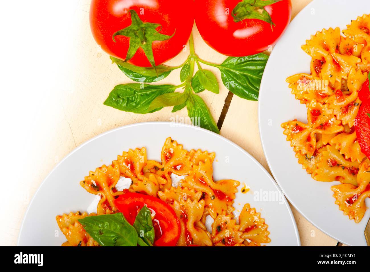Italian pasta farfalle butterfly bow-tie with tomato basil sauce over white rustic wood table ...