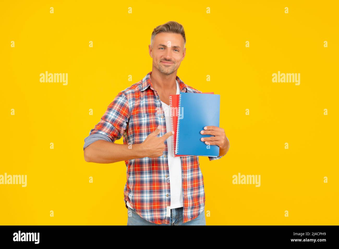 Happy guy student pointing finger at books yellow background, education ...