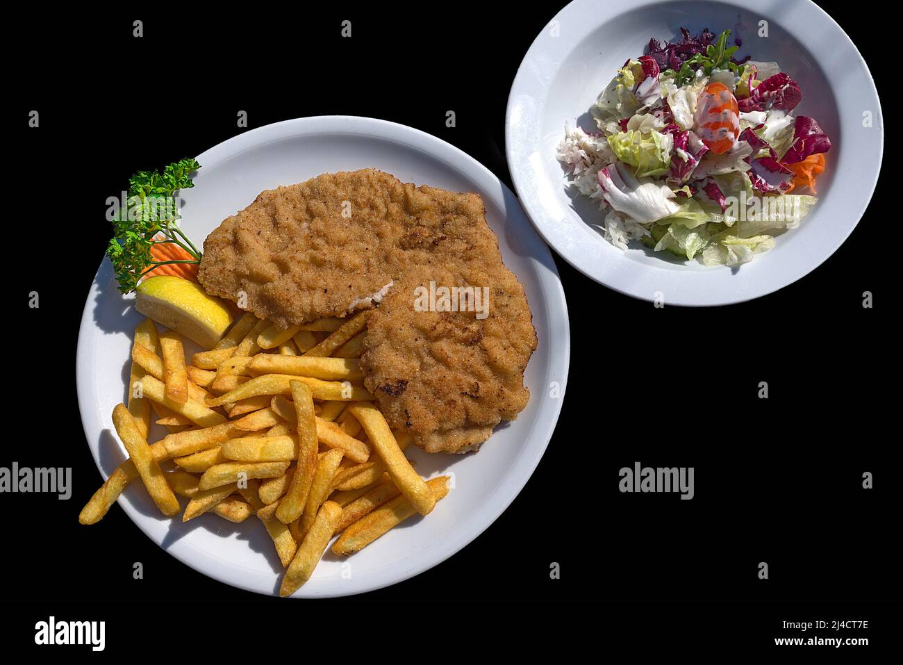Wiener Schnitzel with french fries and salad on a black background ...
