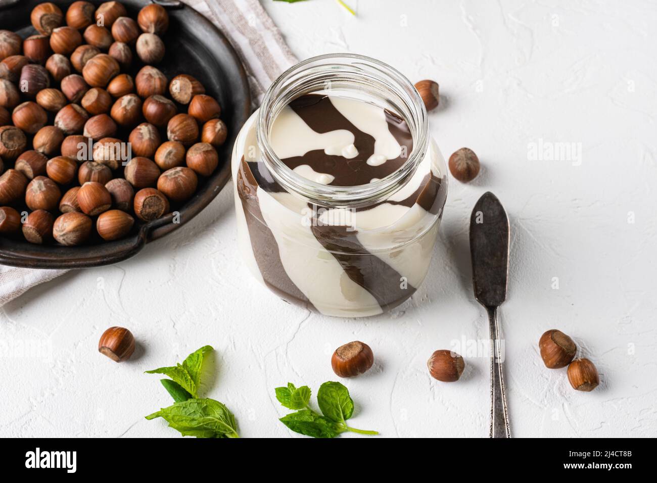 Chocolate spread or nougat cream with hazelnut set, on white stone table background, with copy ...