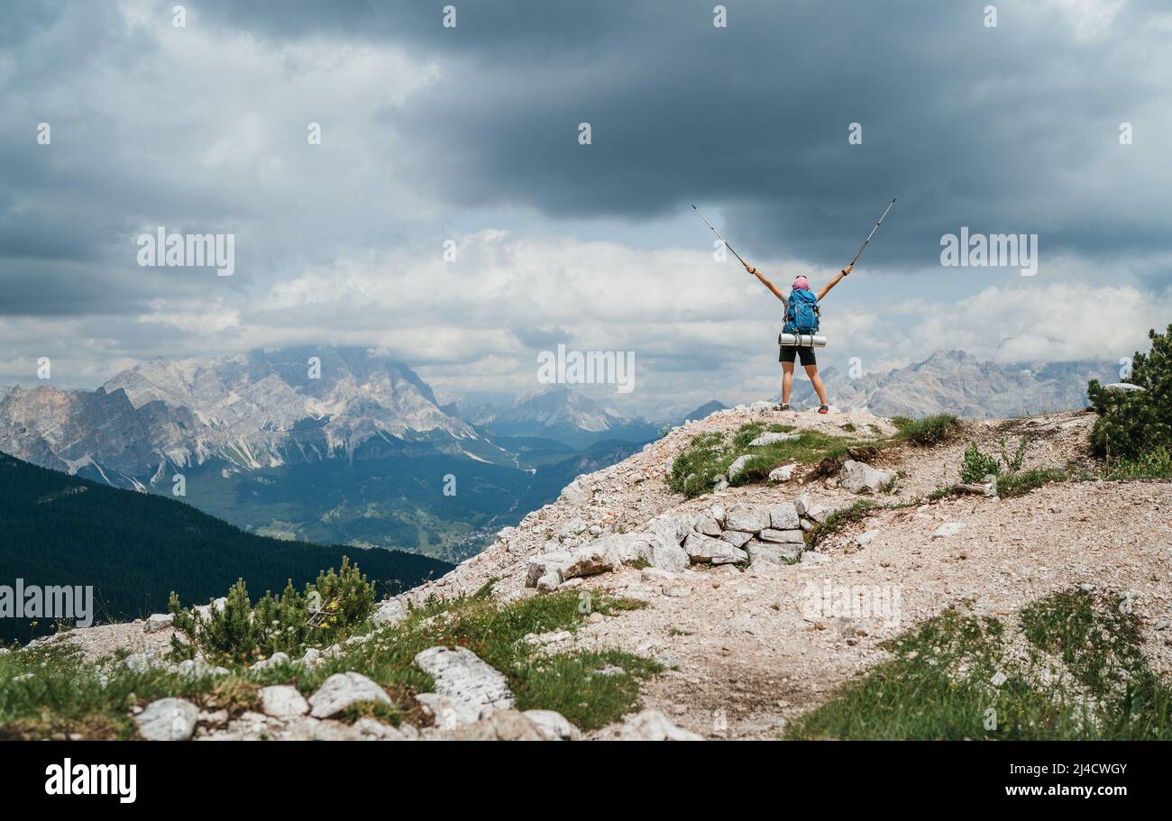 Woman trekker with backpack rose arms up with trekking poles enjoying ...