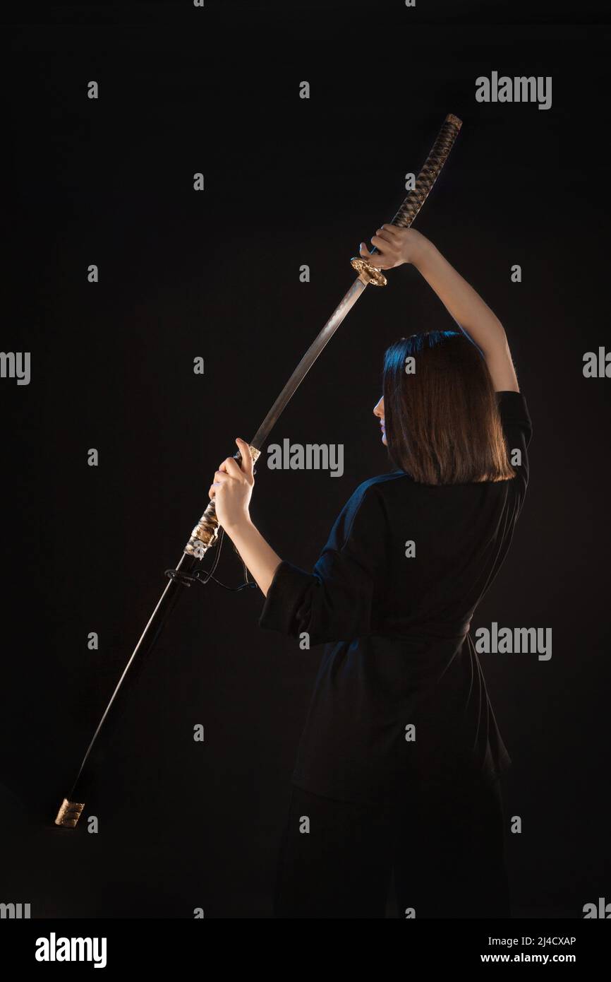 A young beautiful woman in a black kimono draws a Japanese katana from ...