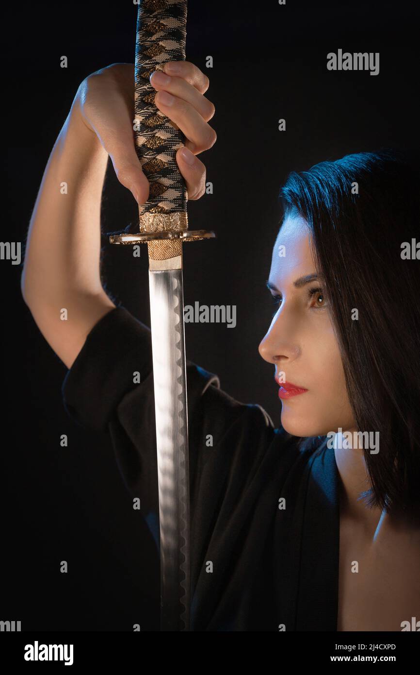 Close-up portrait of a young woman warrior with a katana, looking at a ...