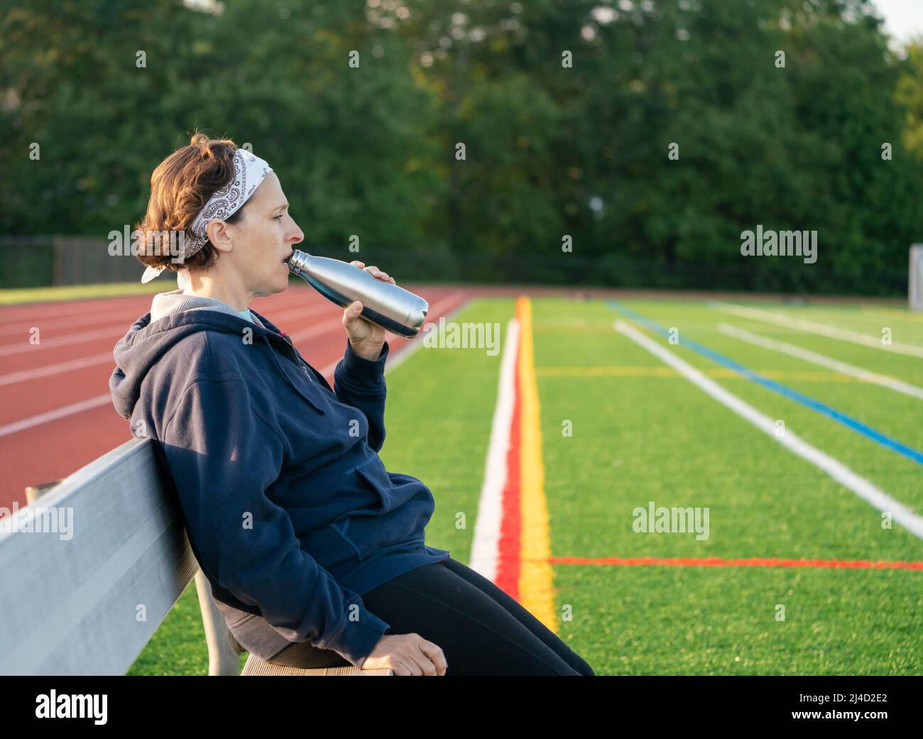 Happy Active middle age woman sitting by a track. Cool down hydration ...