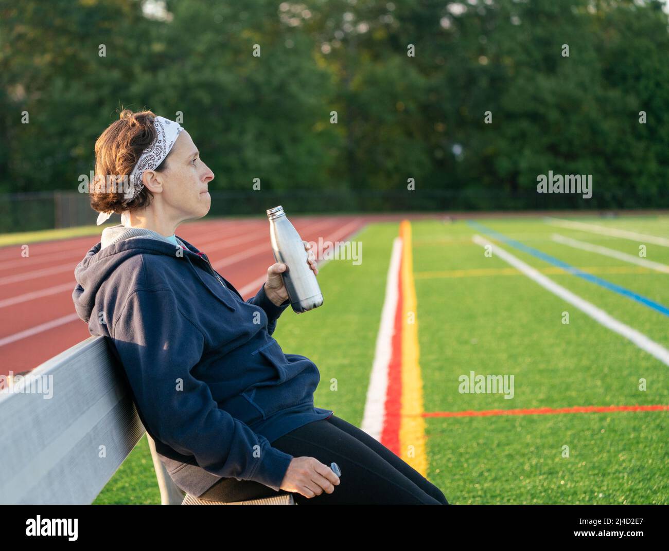 Happy Active middle age woman sitting by a track. Cool down hydration ...