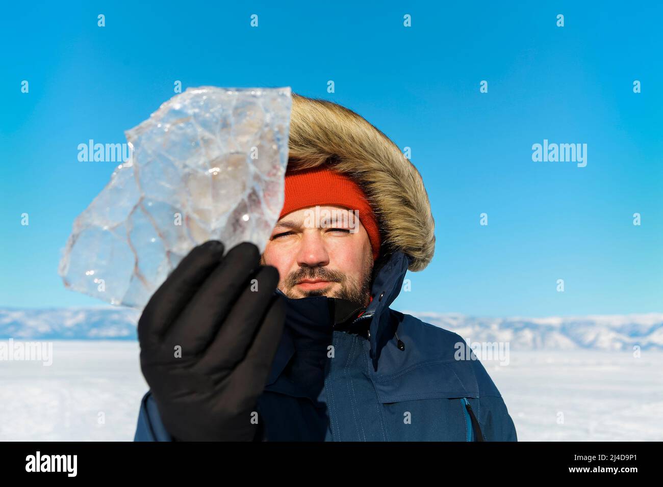 Happy smiling man wearing winter blue jacket and red hat holding piece ...