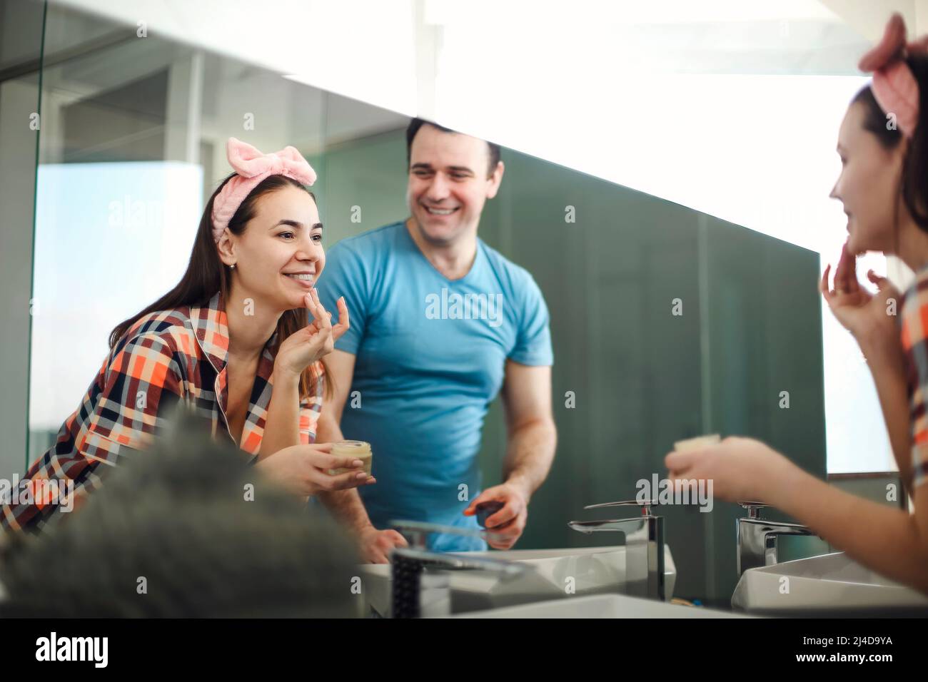 Cheerful Brunette Man Looking At Beautiful Girlfriend Applying Face Cream In Bathroom Getting