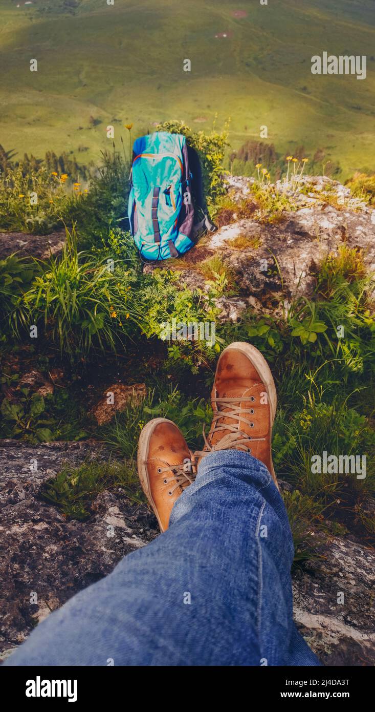 Hiking backpack and legs in sports shoes of young woman resting in a ...