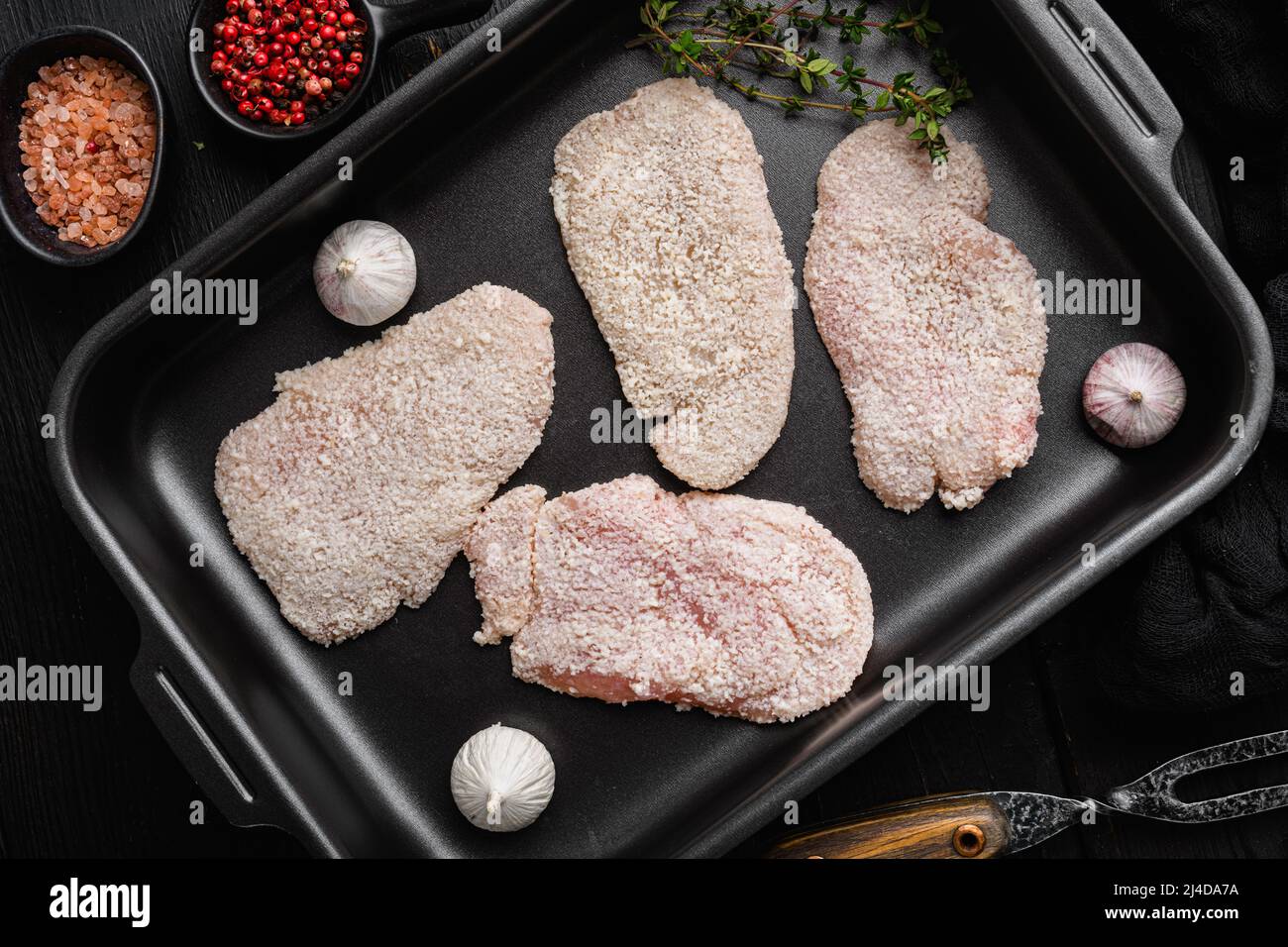 Raw chicken schnitzel in breadcrumbs set, on black wooden table ...