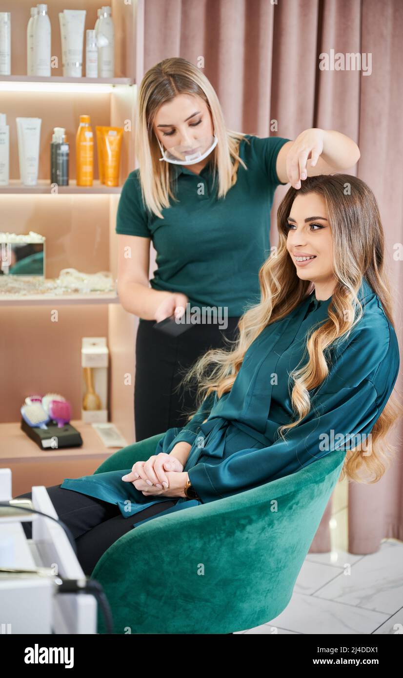 Young woman with long hair sitting in salon chair while hairdresser ...