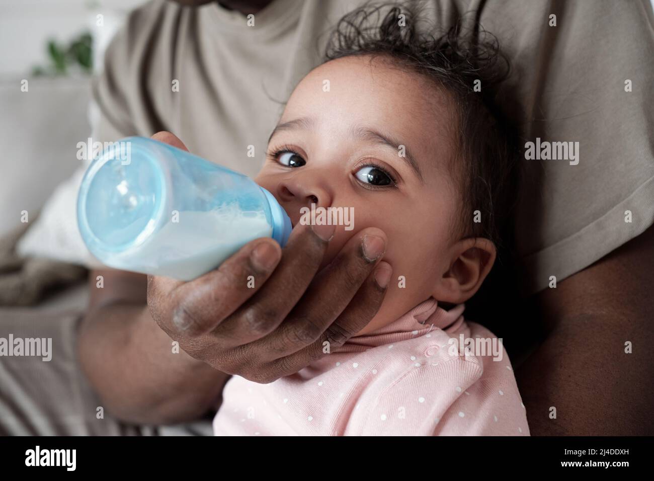 Close-up portrait of unrecognizable Black man bottle feeding his baby ...