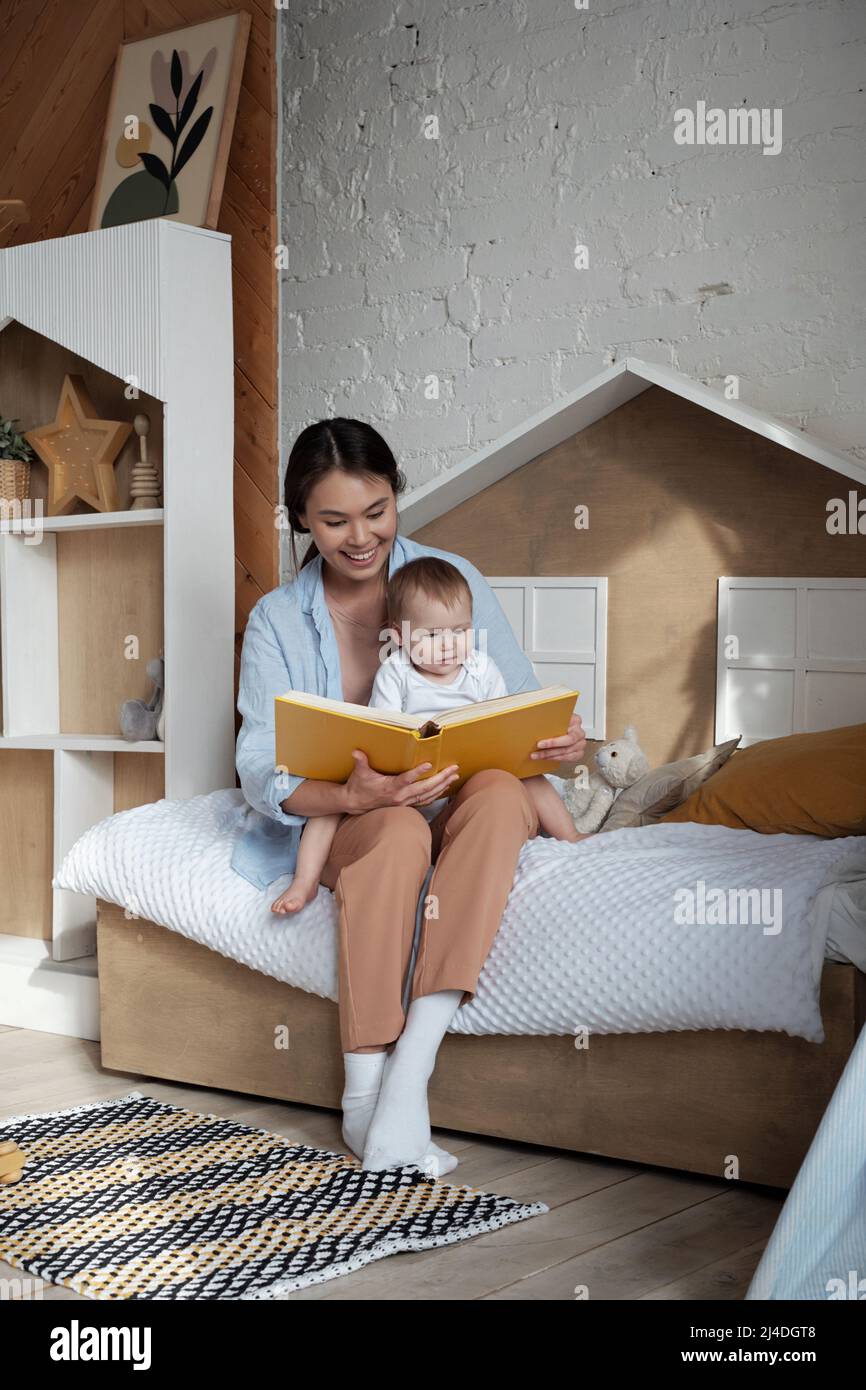 Modern happy young mother sitting in cozy kids room with baby daughter ...