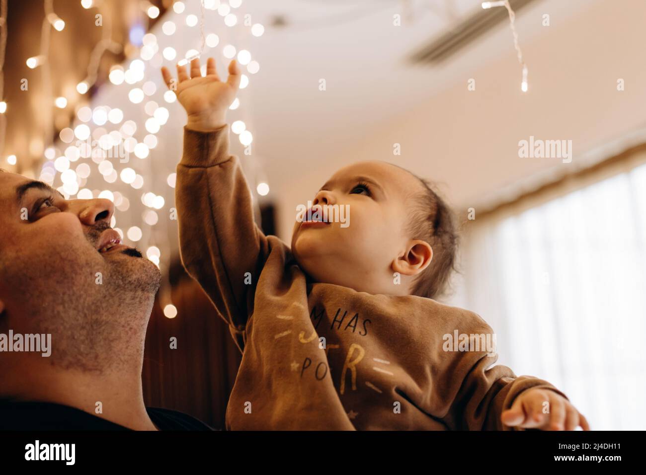 Father and son playing with lights garland. Dad holds his baby boy on ...