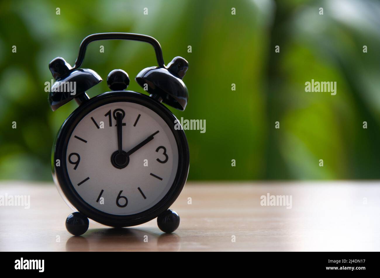 Black alarm clock isolated on blurred nature background. The clock set ...