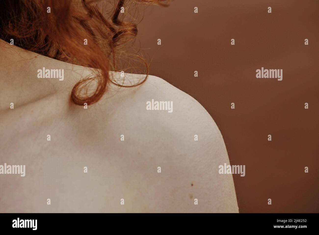 Close-up of young woman with red curly hair reaching to her shoulder ...