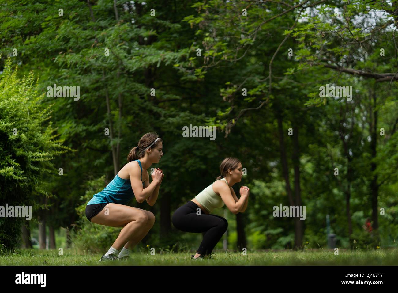 Two attractive and beautiful girls are doing some squats out in nature ...