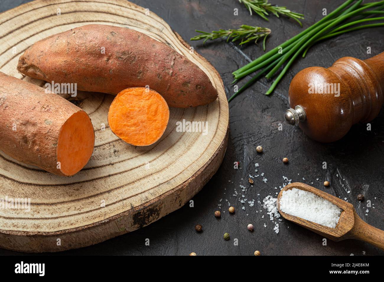 Raw sweet potatoes, organic yam on a cutting board and spices on a dark ...