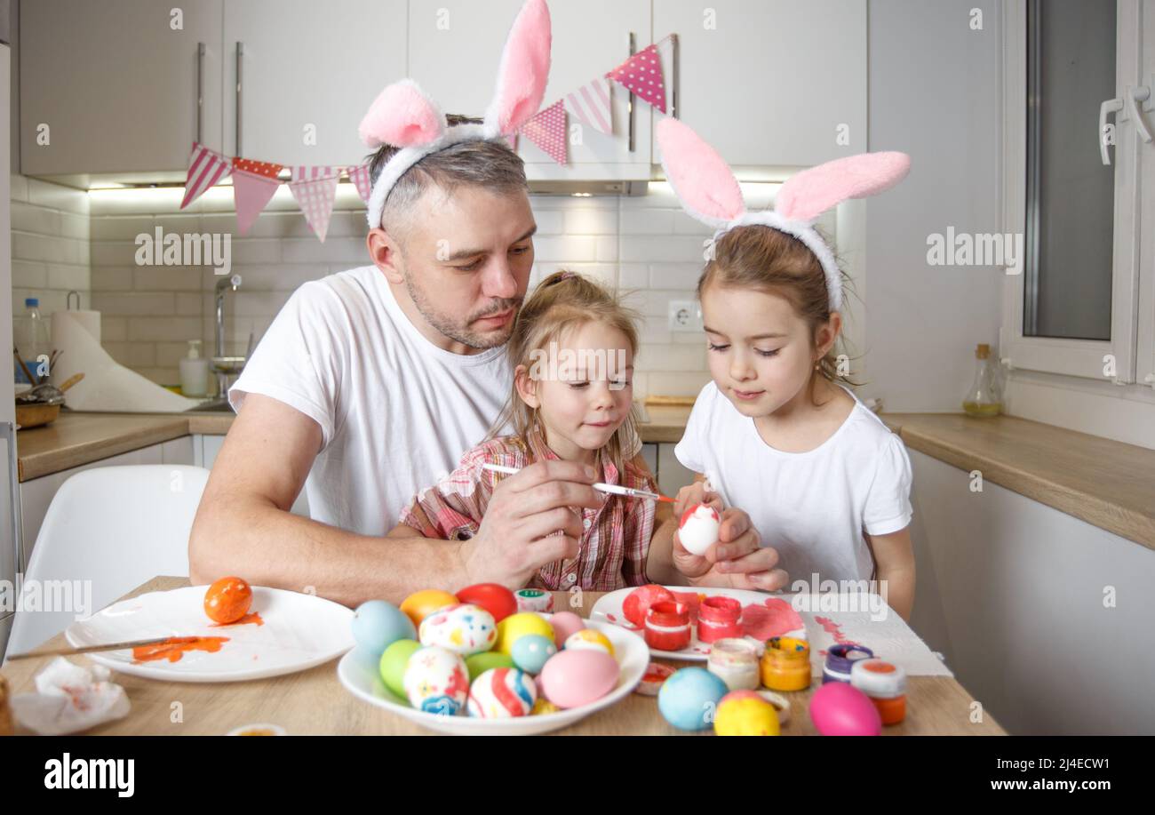 a happy father with two young daughters paints Easter eggs and prepares ...