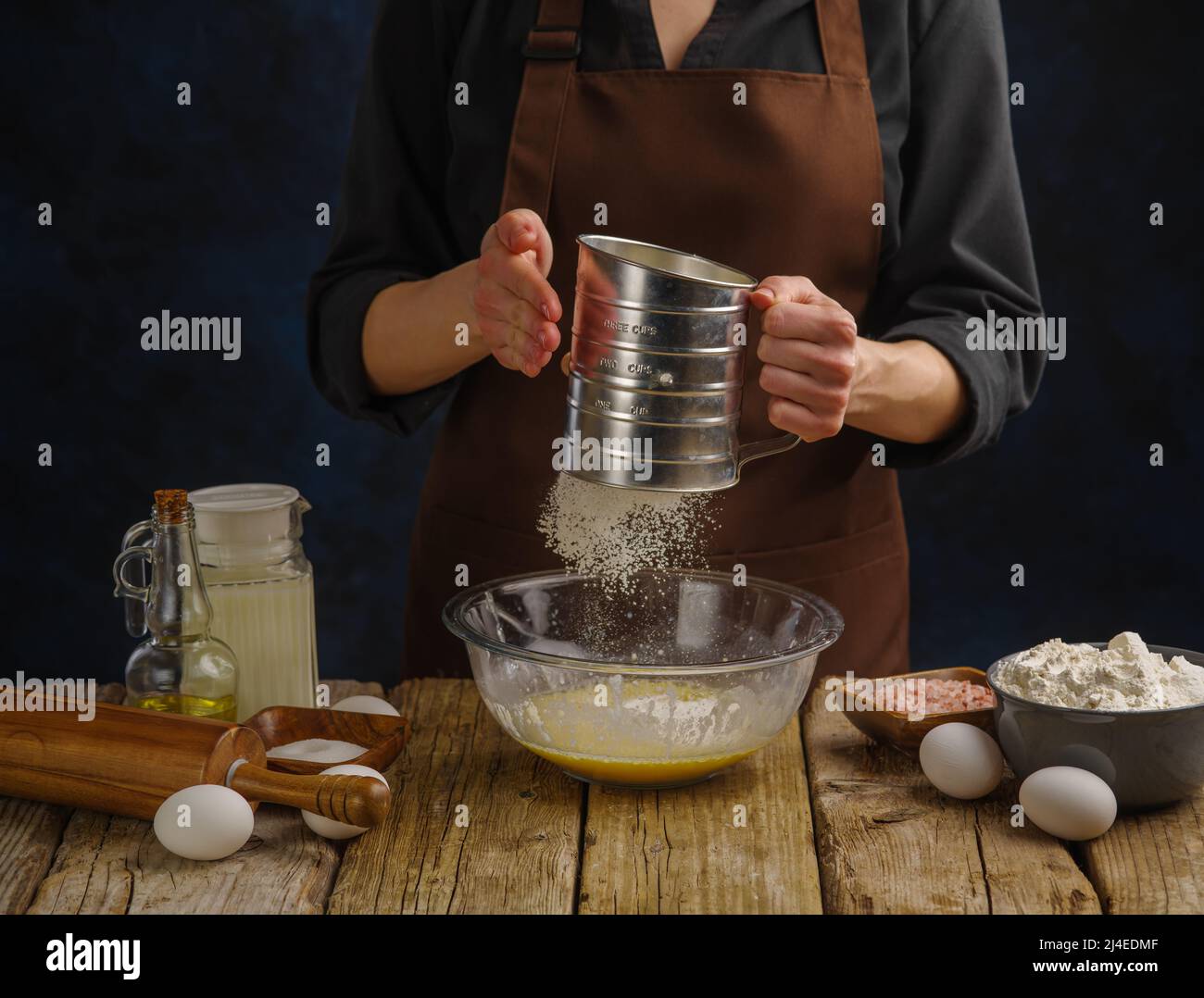A professional chef prepares dough on a wooden kitchen table. Sifts ...