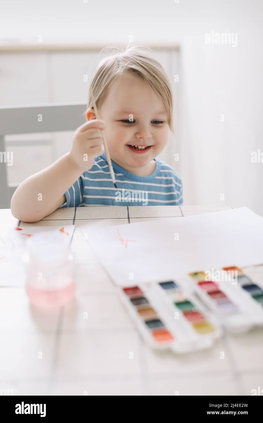 Child painting and drawing with watercolor paint at white table ...