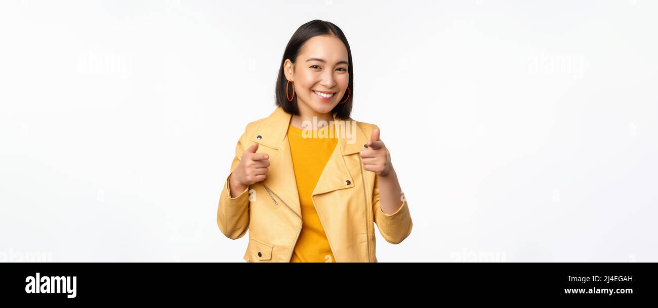 Hey you. Happy smiling asian woman pointing fingers at camera, choosing ...