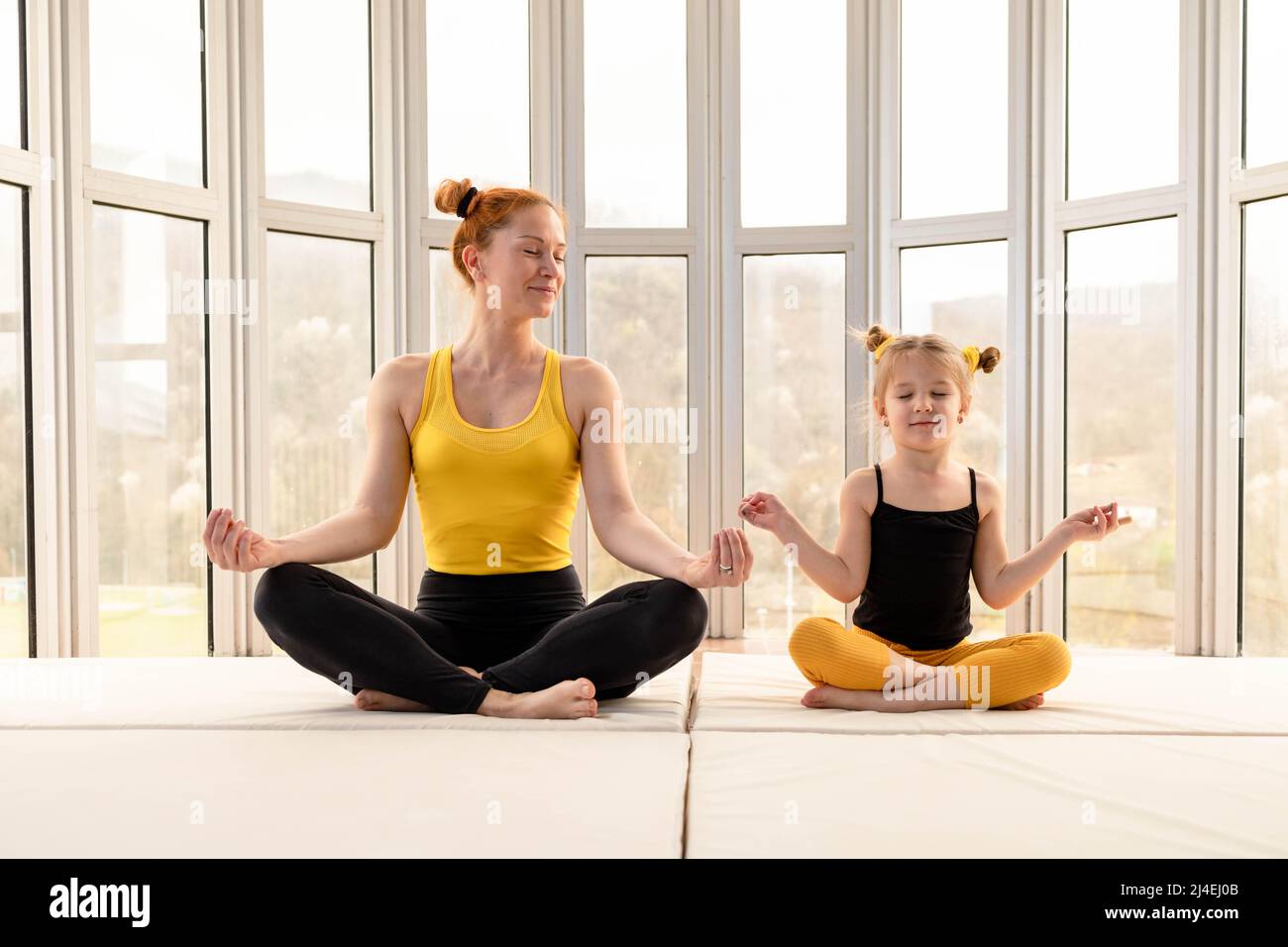 Young Mother And Daughter Practicing Yoga Together Meditating Stock