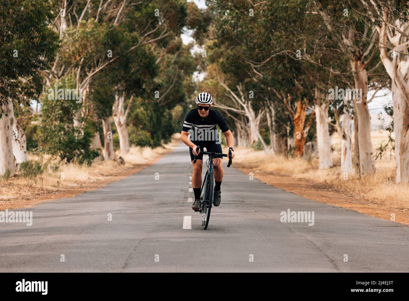 Sportswoman riding a bicycle in the center of an empty road ...