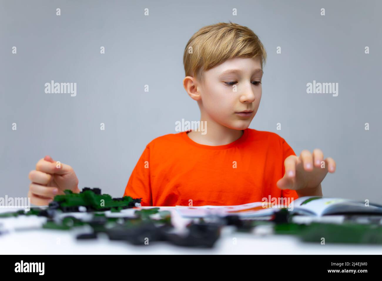 a boy plays with a plastic constructor studies instructions for ...