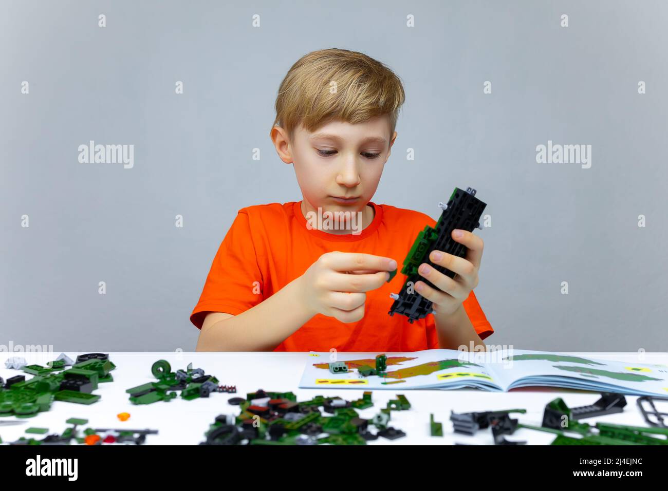 a boy at the table plays with a plastic constructor holds a finished ...