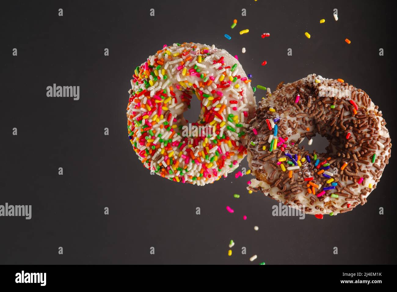 Two multi-colored donuts decorated with icing sugar and confectionery ...