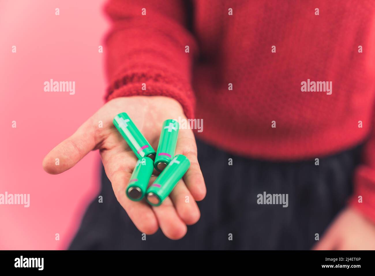 Palm of a caucasian person in a red sweater holding four batteries over ...