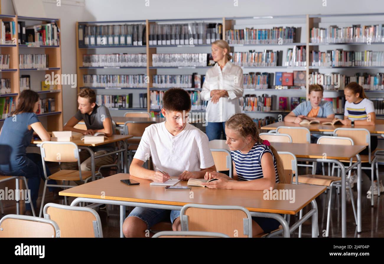 Schoolchildren preparing for lesson in school library, reading and ...