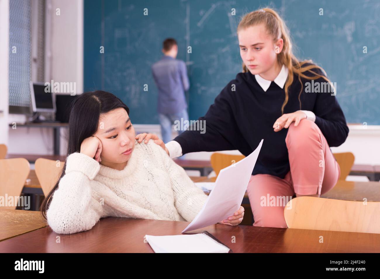 Teen female student supporting upset Chinese girl in classroom Stock ...