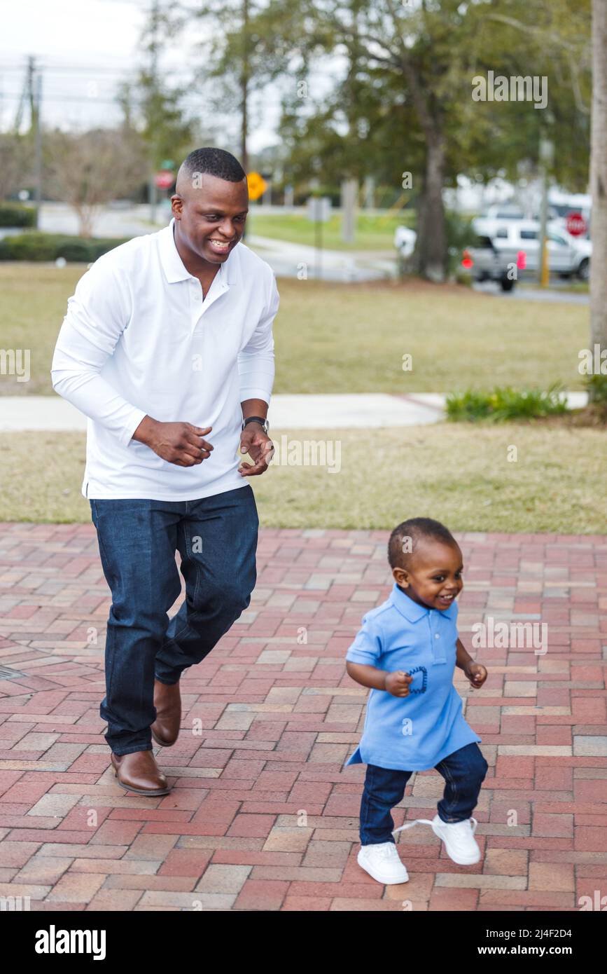 A dad chasing his toddler son around outdoors while they are playing ...