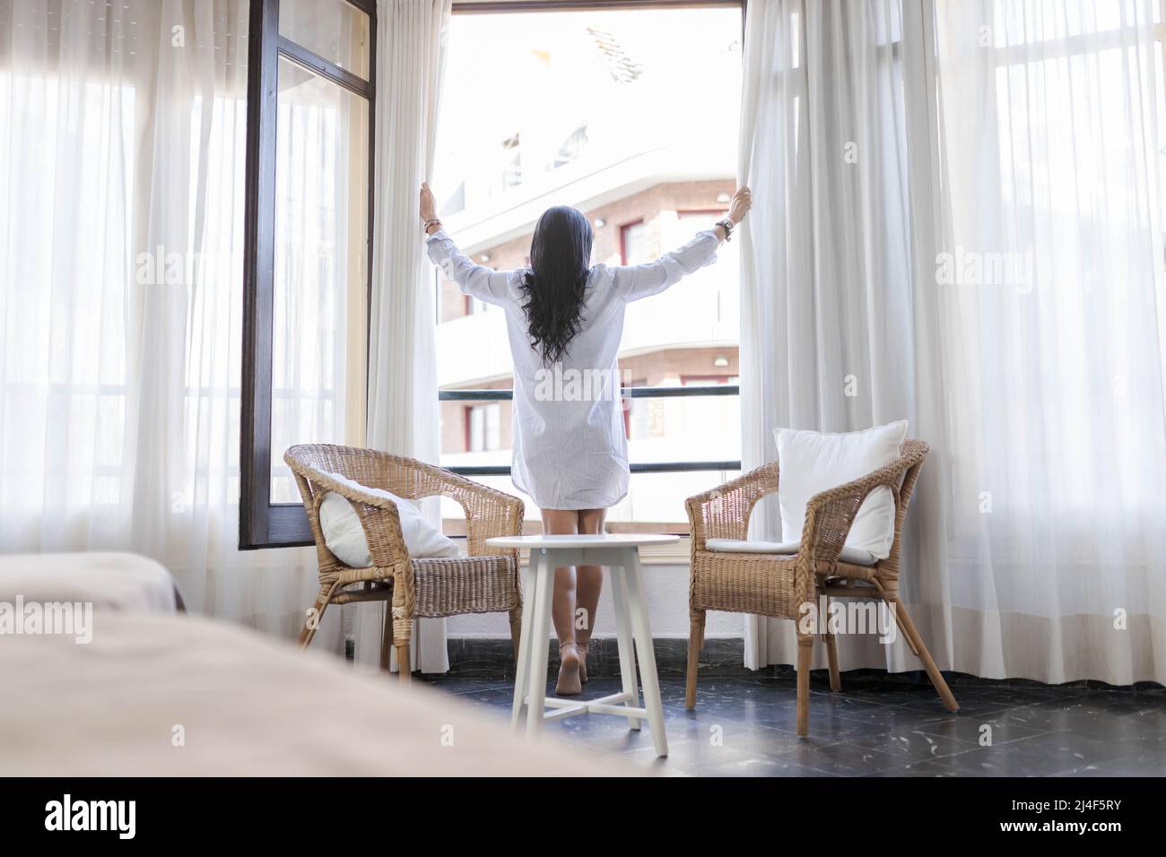 Happy rich young woman wear night robe stand at big window open lace curtains in bedroom look ...