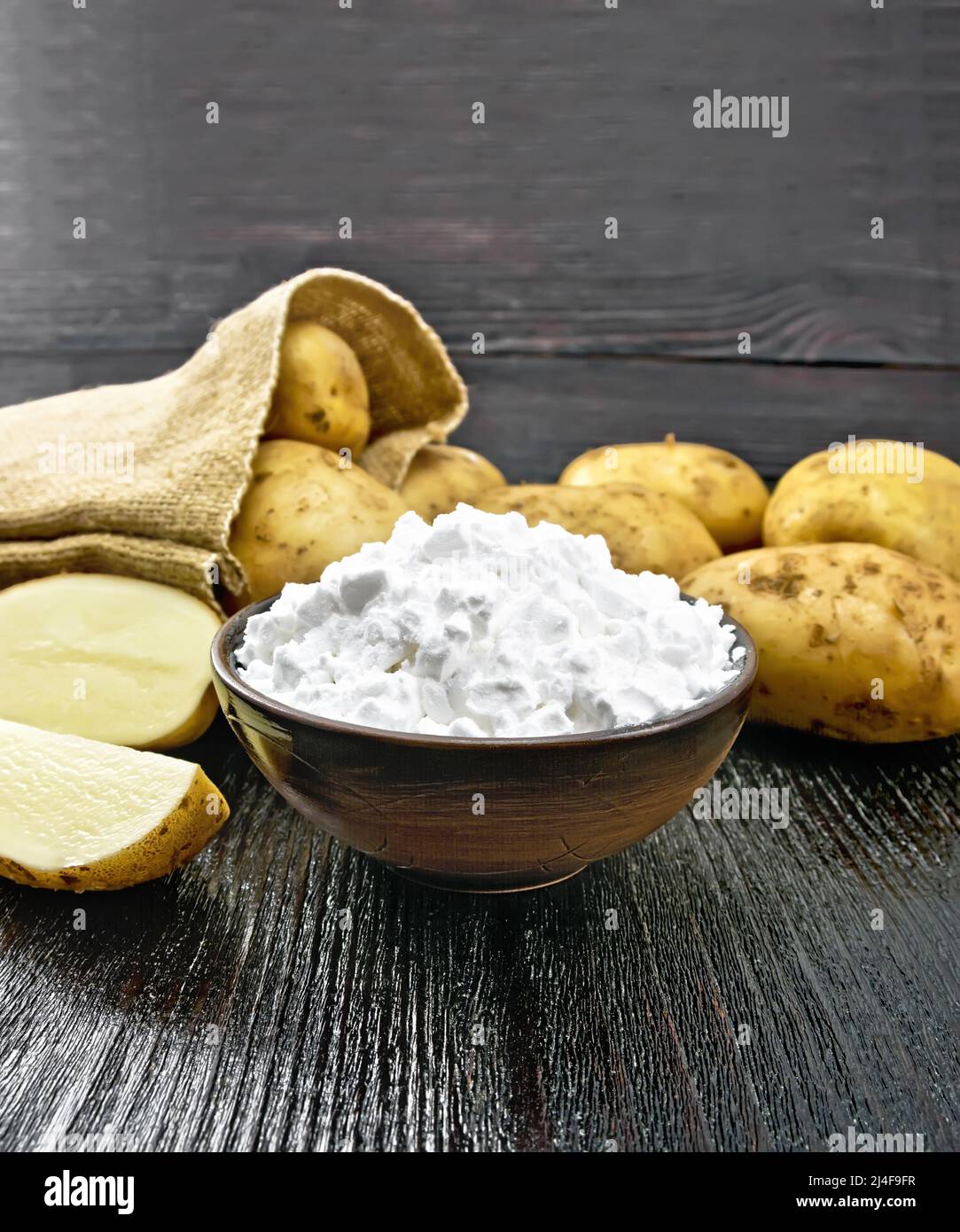 Potato starch in clay bowl, vegetable tubers in a bag and on the table ...