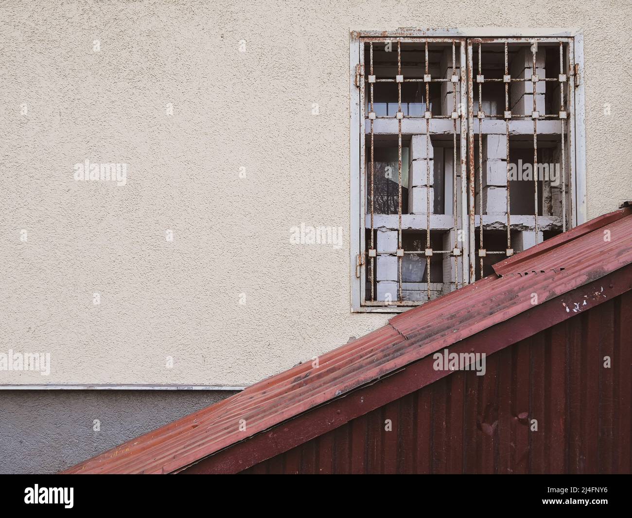 A yellow wall on which an old dirty window with a metal grill is ...